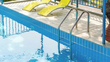 Piscina com azulejos azuis, escadas de metal e cadeiras de descanso amarelas.