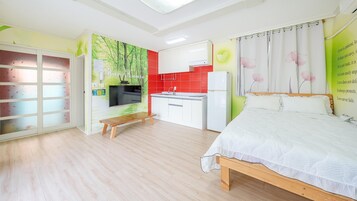 Quarto com cama, televisão, pequena cozinha e porta deslizante.