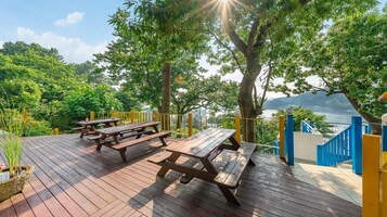 Um deck de madeira com mesas de piquenique, com vista para um cenário com água e vegetação.