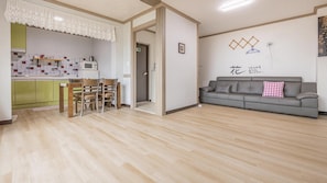 Sala de estar com sofá cinza, piso de madeira e cozinha com micro-ondas e cadeiras.