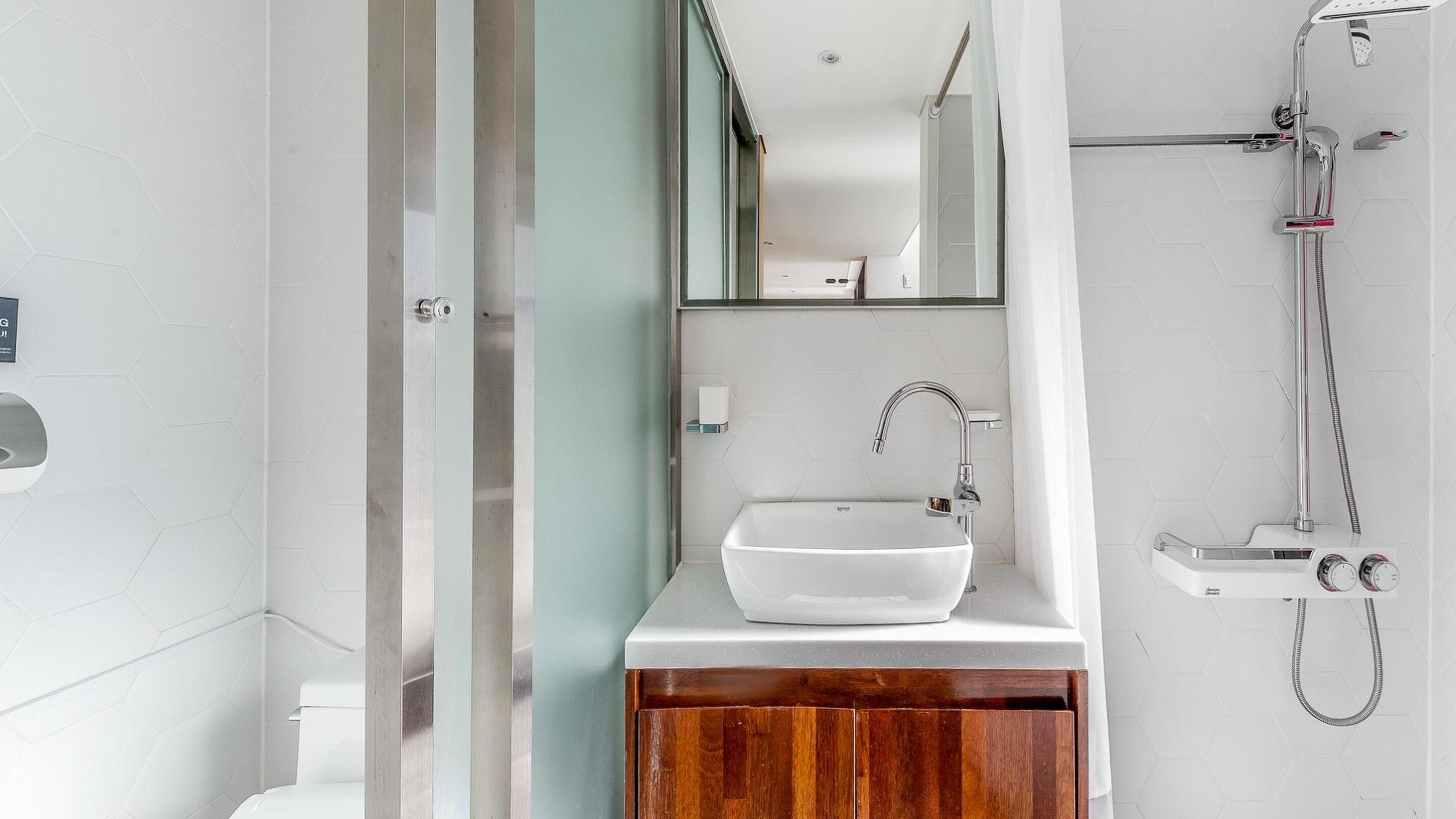 Uma casa de banho moderna com lavatório branco, espelho e chuveiro.