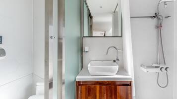 Uma casa de banho moderna com lavatório branco, espelho e chuveiro.