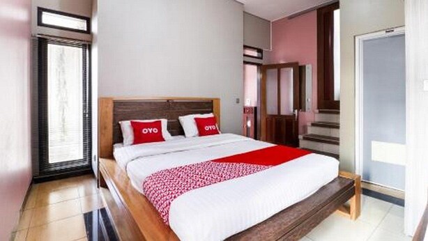 Quarto de hotel moderno com uma cama grande, cabeceira de madeira e colcha estampada em vermelho e branco.
