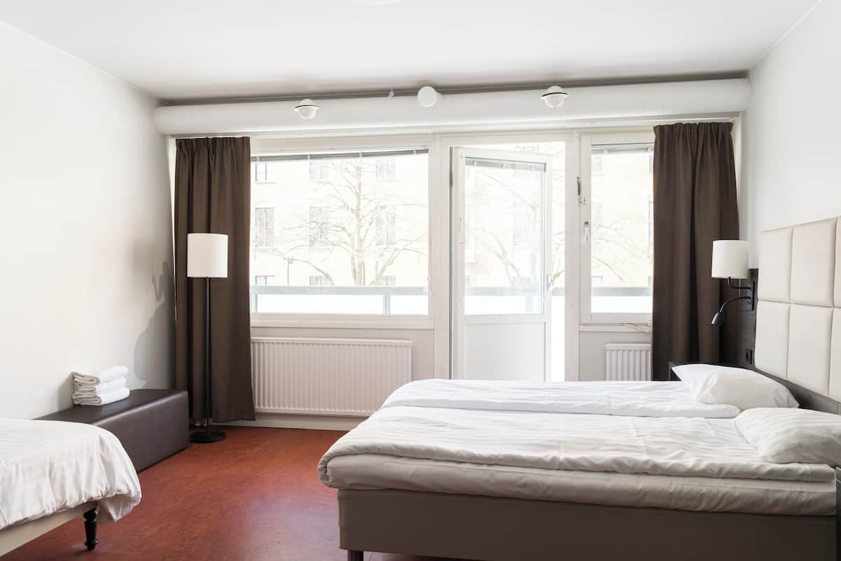 Quarto de hotel com cama, um banco, janela e radiador.