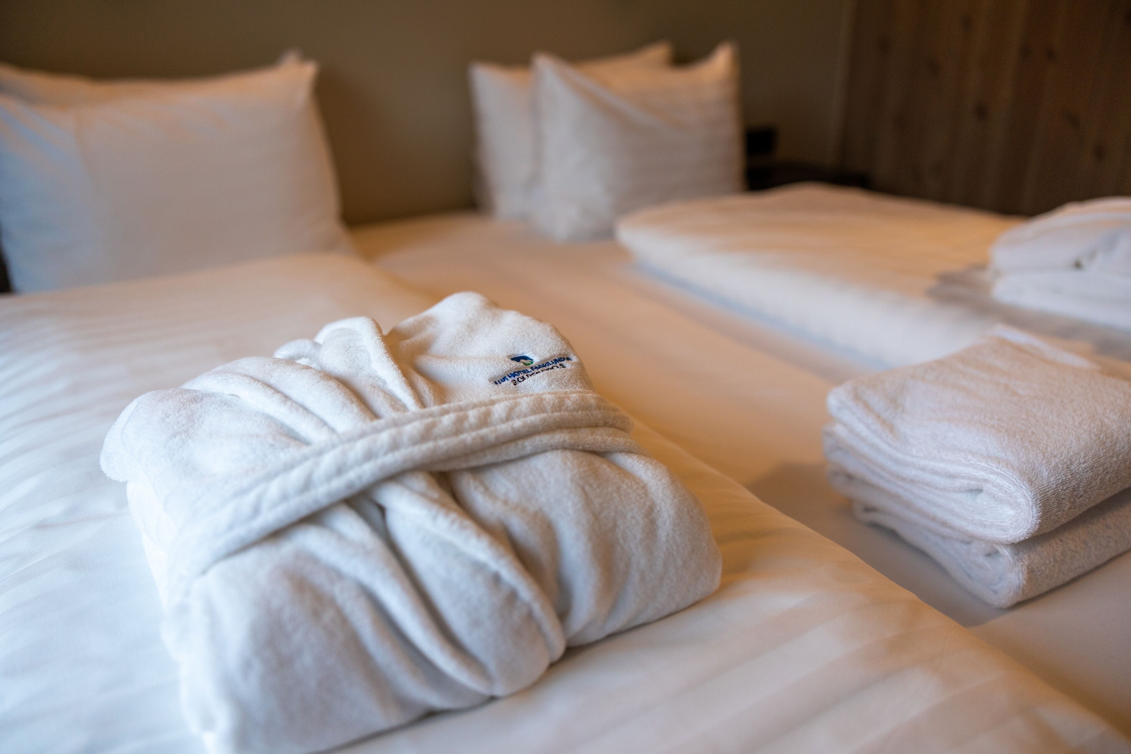 Quarto de hotel com camas bem arrumadas, cada uma com toalha dobrada e roupão enrolado.