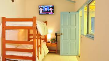 Quarto com beliche, escrivaninha com luminária, televisão fixada na parede e porta que dá para outro quarto.