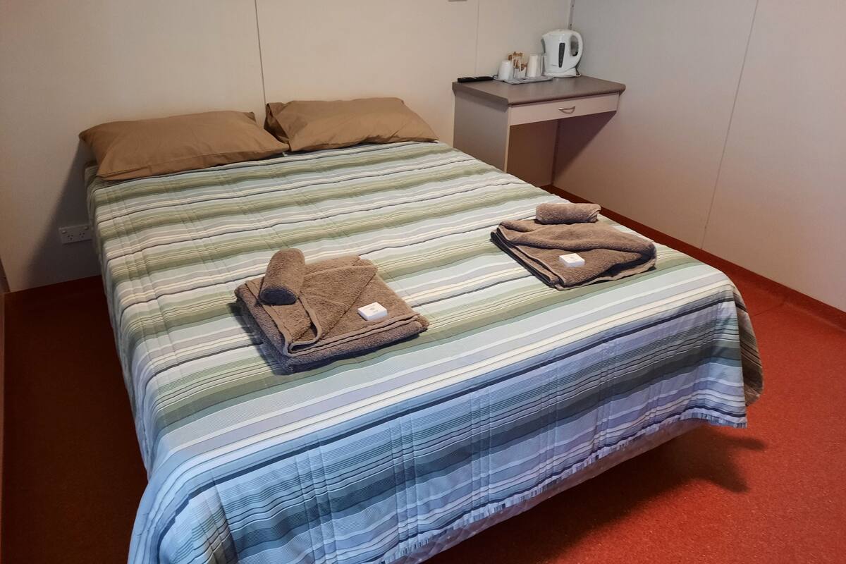 Uma cama bem arrumada com roupa de cama listrada, um travesseiro marrom e duas toalhas dobradas sobre a cama.
