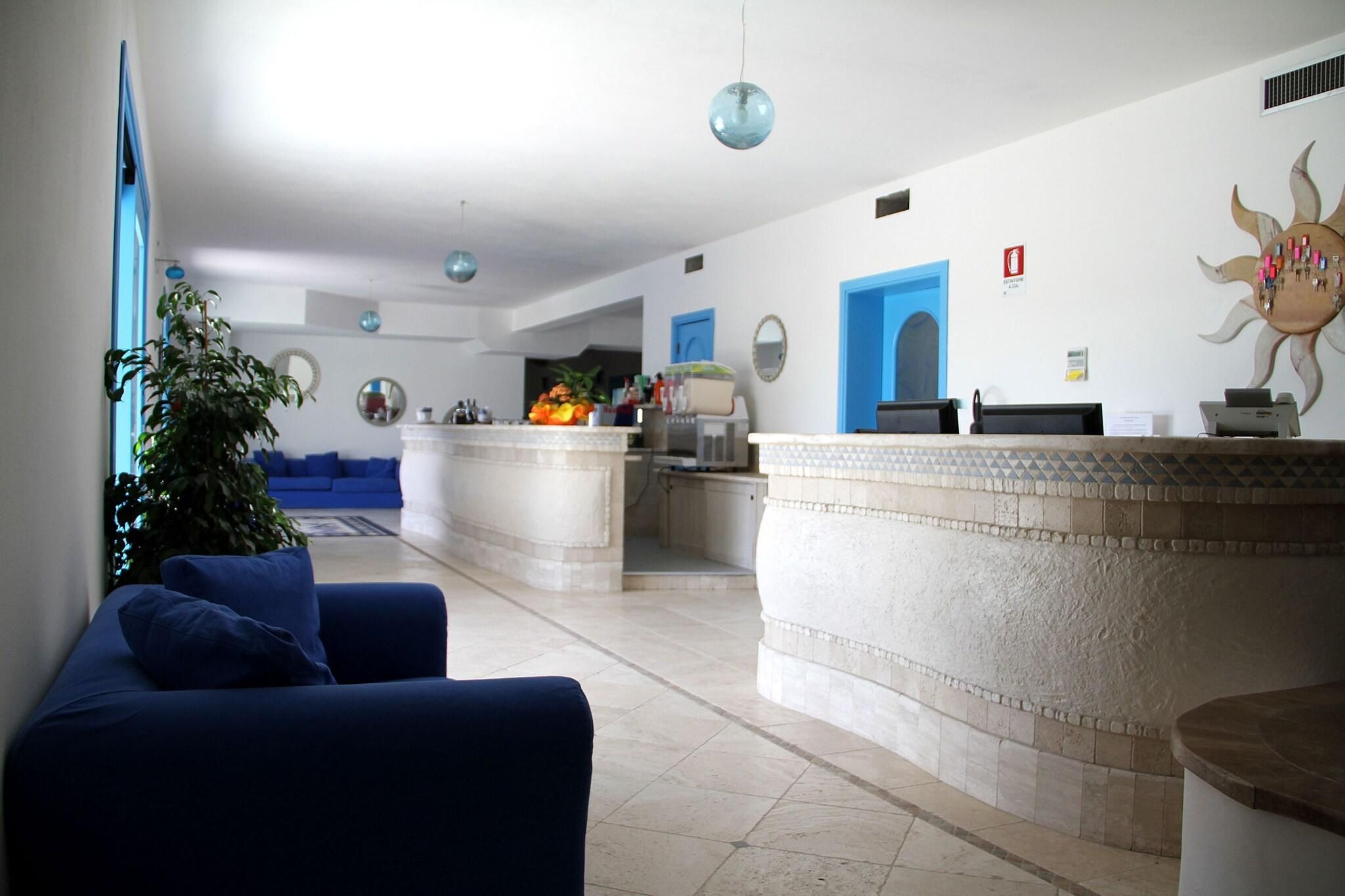 Uma área de recepção com um sofá azul, um balcão de atendimento, um espelho grande e um painel decorativo em formato de sol.