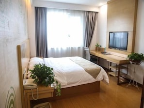 Quarto de hotel com cama, escrivaninha, televisão e janela com cortinas.