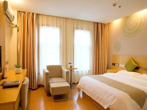 Quarto de hotel com uma cama, uma escrivaninha, uma cadeira e uma mesinha.