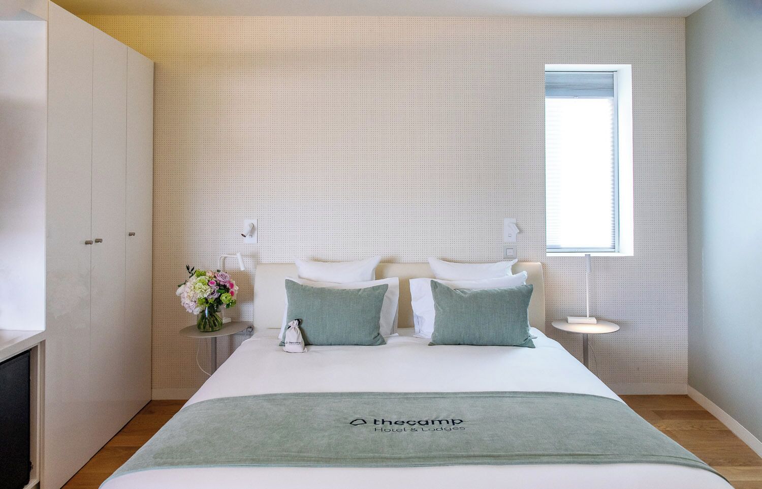 Quarto de hotel com cama, mesa de cabeceira, janela e guarda-roupa.