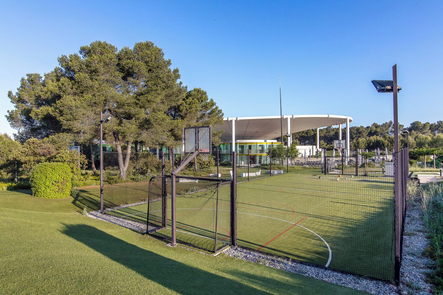 Uma instalação esportiva com quadra de tênis, área de estar coberta e um edifício ao fundo.
