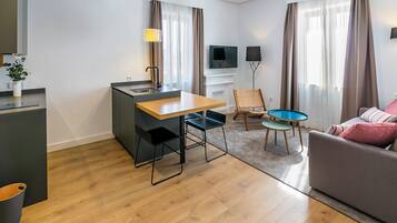 Quarto de hotel moderno com uma mesa de jantar de madeira, um sofá, uma televisão e uma pequena mesa com cadeiras.