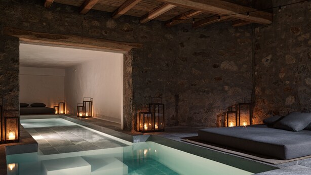 Uma área de spa com piscina, paredes de pedra, vigas de madeira e assentos.