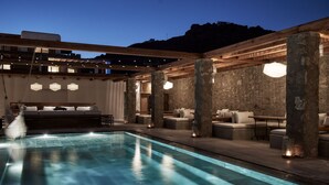 Uma área de piscina com bar, assentos, pilares de pedra e luminárias pendentes.