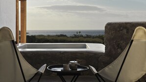 Varanda com duas cadeiras e uma mesa pequena, com vista para a paisagem costeira, o mar e o verde.