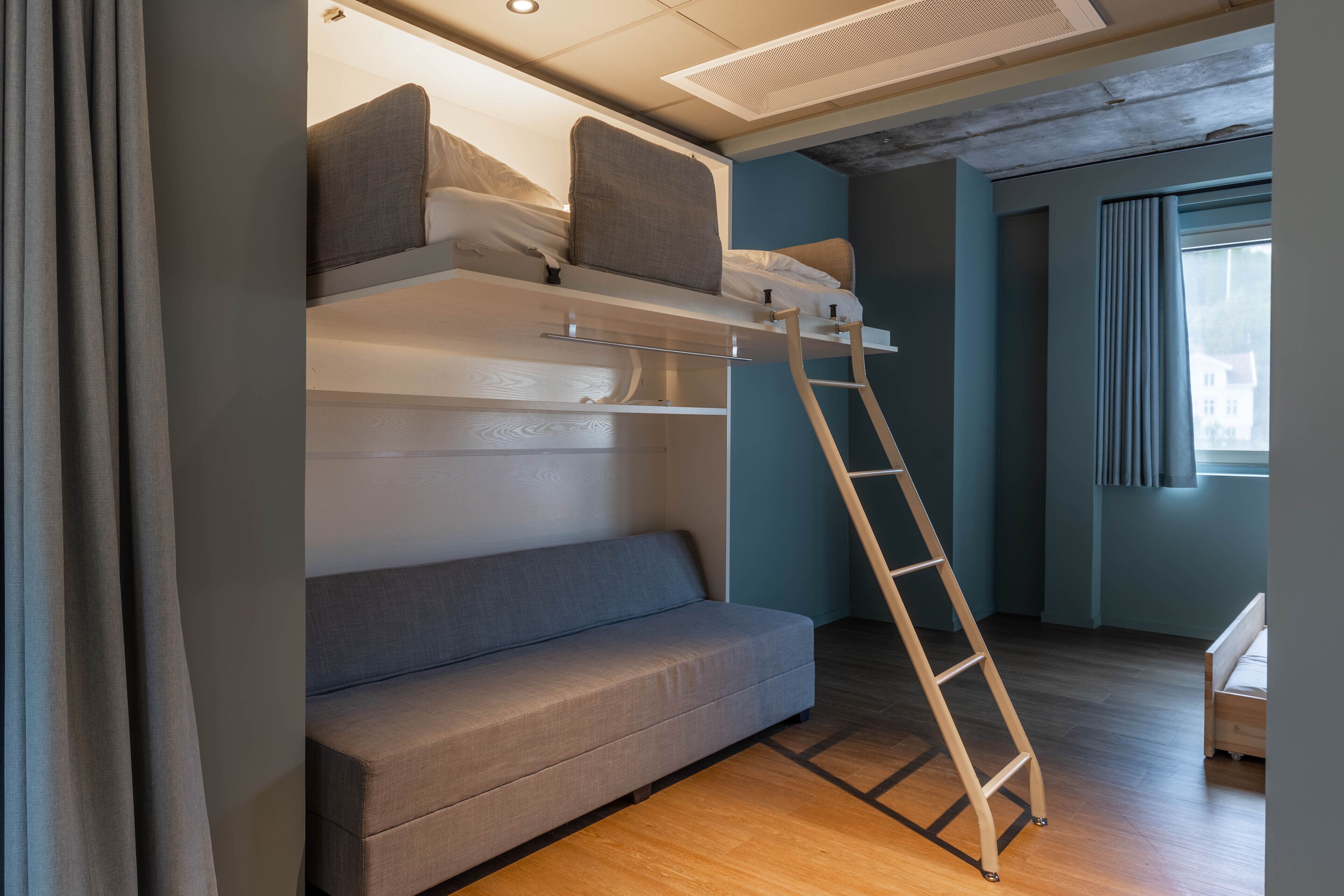 Uma cama beliche com escada, um sofá e uma janela com cortinas.