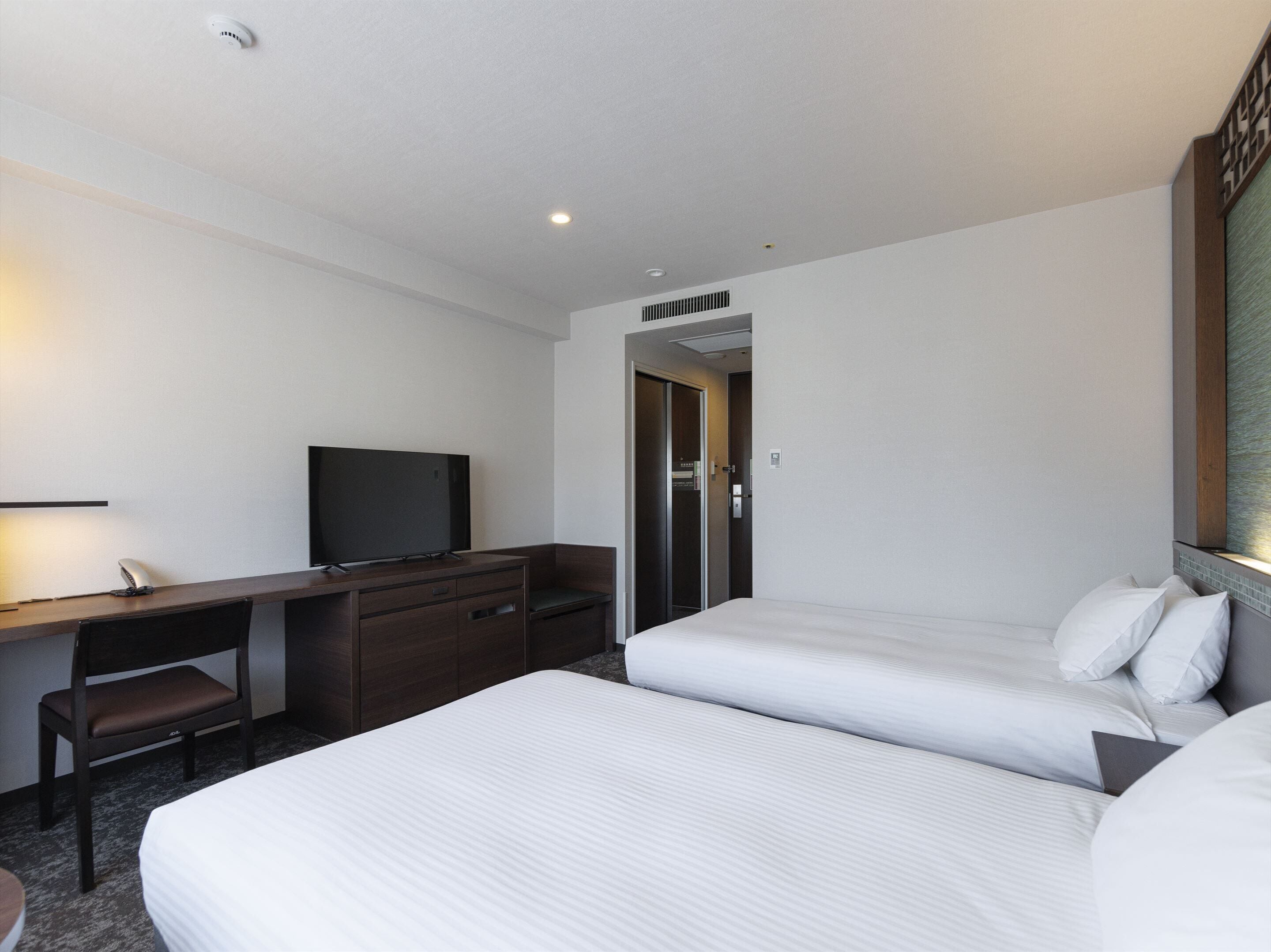 Quarto de hotel com duas camas, uma mesa de trabalho, televisão e porta para o banheiro.