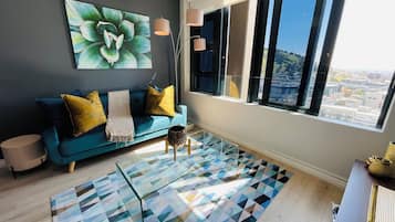 Uma sala de estar moderna com um sofá azul-turquesa, tapete estampado e uma grande janela com vista para a cidade.