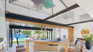 Uma cozinha moderna com uma ilha grande, vista para uma piscina e uma área de refeições com uma cadeira e uma planta.