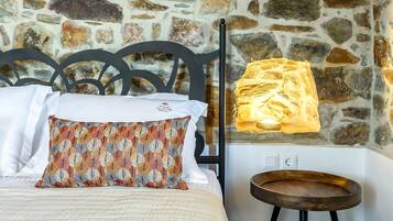Quarto com parede de pedra, cama com roupa de cama estampada, mesa de cabeceira e luminária.