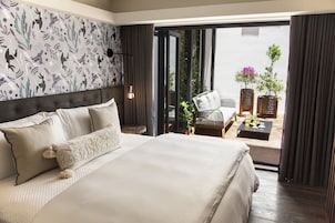 Quarto com uma cama grande, mesa de cabeceira, uma cadeira e uma mesa com uma planta e uma garrafa.