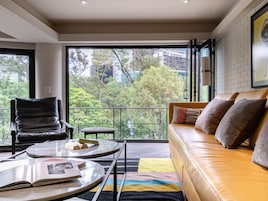 Uma sala de estar moderna com um sofá de couro, uma poltrona de couro preta e uma mesinha redonda com livros e um prato.