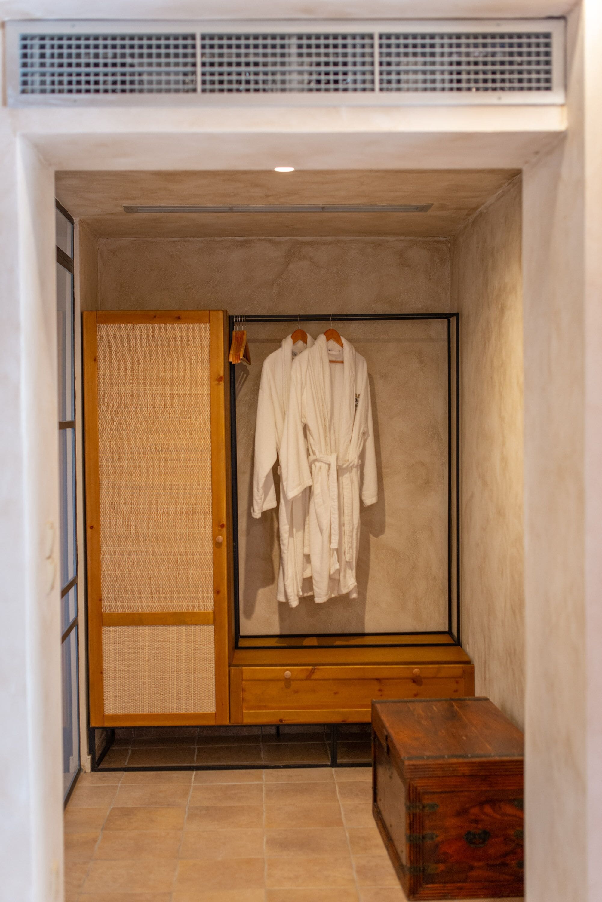 Um quarto com um banco de madeira, um baú de madeira e uma porta deslizante com um tapete tecido.