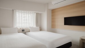 Quarto de hotel com duas camas, uma televisão presa na parede e uma janela com cortinas.