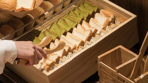 Uma banca de madeira com diversos tipos de pão, incluindo variedades verdes e brancas.
