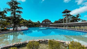 Uma grande piscina ao ar livre rodeada por palmeiras e um edifício com telhado de palha.