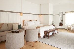 Quarto de hotel moderno com uma cama grande, um sofá, uma cadeira, uma mesinha e um espelho.