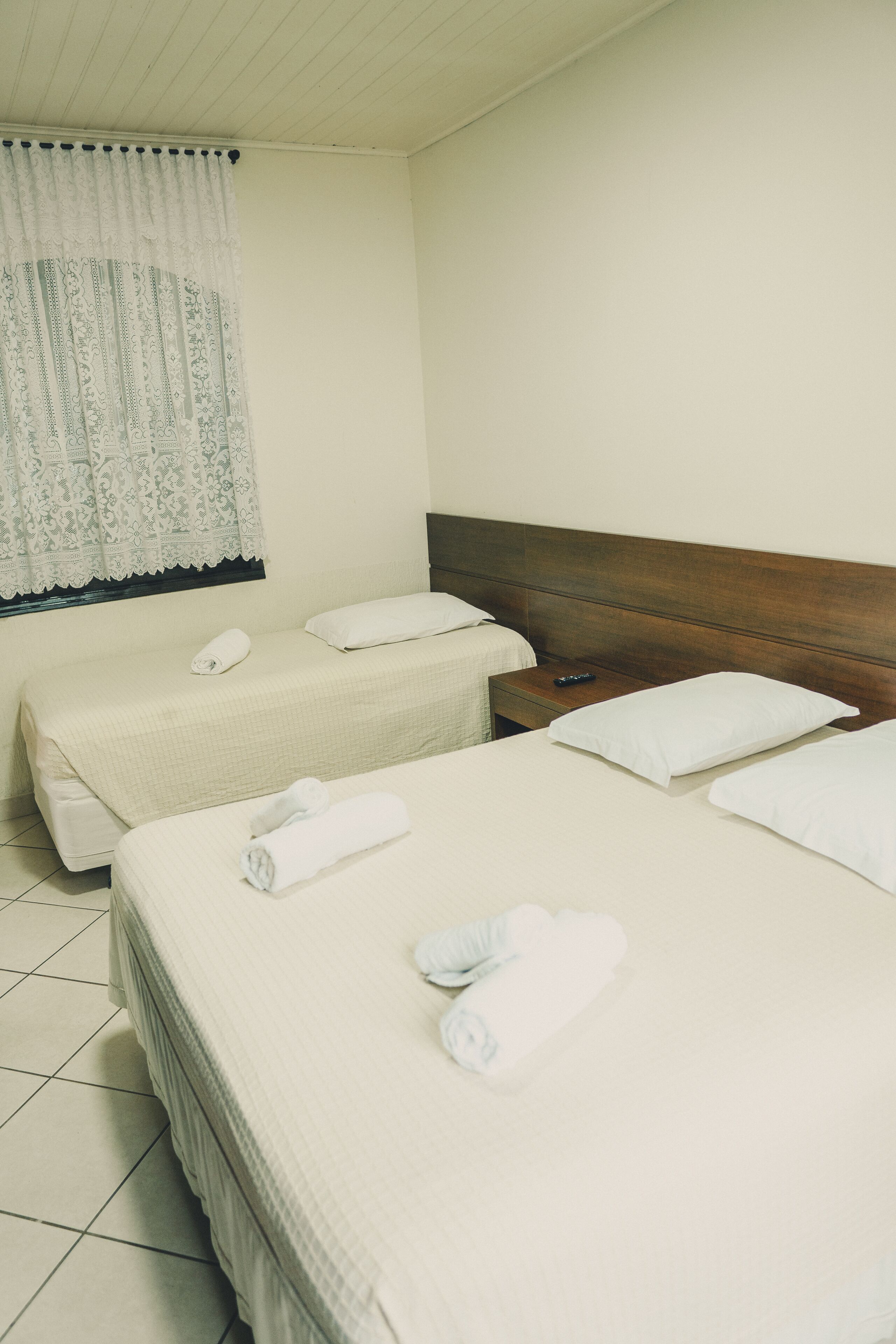 Quarto de hotel com duas camas, cada uma com um travesseiro e uma toalha enrolada.