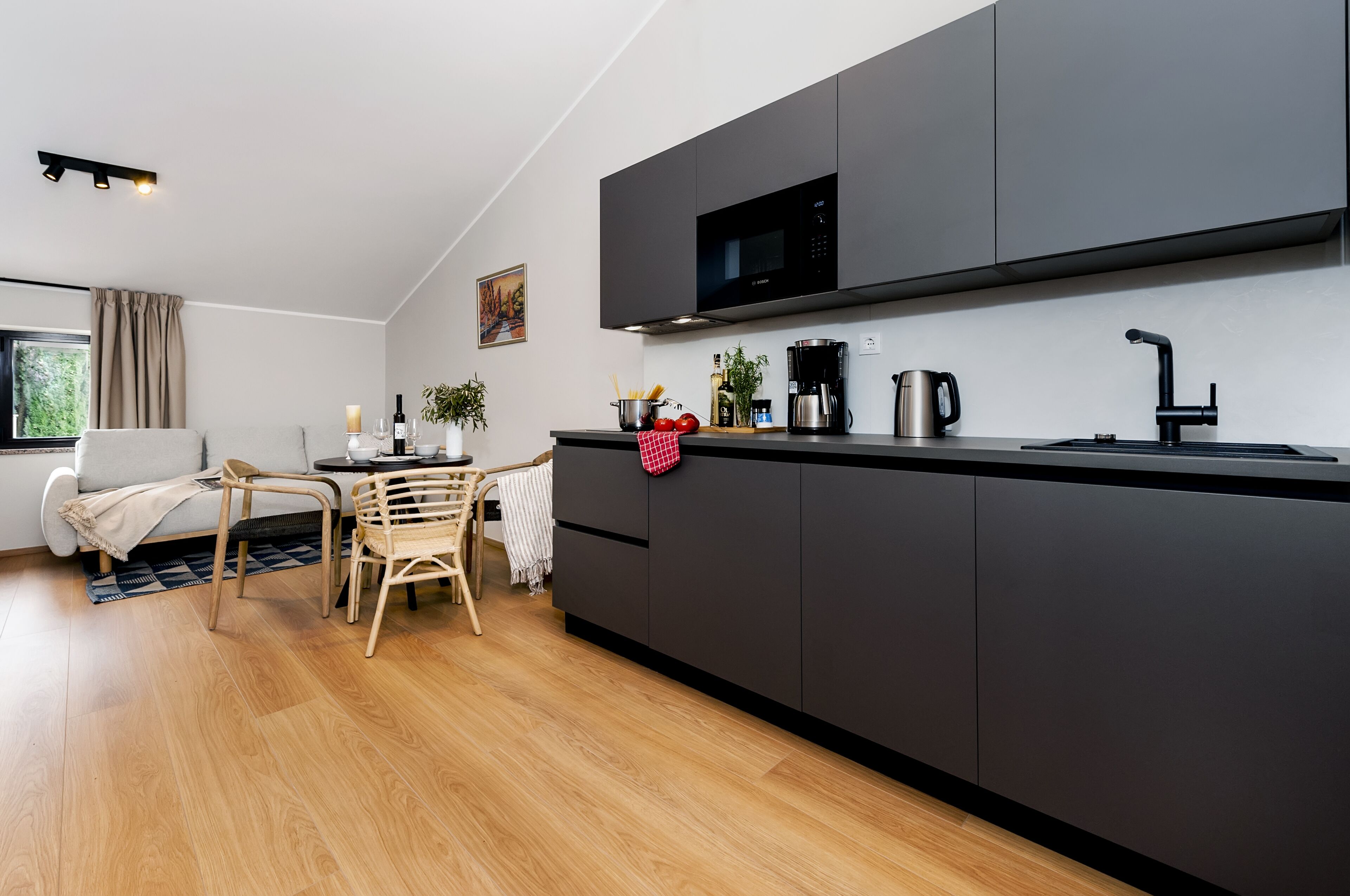 Cozinha moderna com armários escuros, micro-ondas e cafeteira. Possui uma área de refeições com mesa e cadeiras.