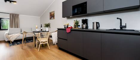 Cozinha moderna com armários escuros, micro-ondas e cafeteira. Possui uma área de refeições com mesa e cadeiras.