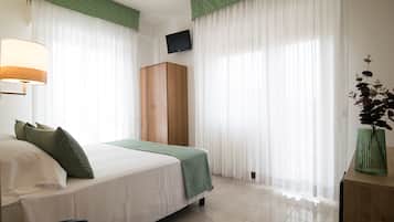 Quarto de hotel com cama, guarda-roupa de madeira, televisão na parede e um vaso com flores sobre uma mesa de apoio.