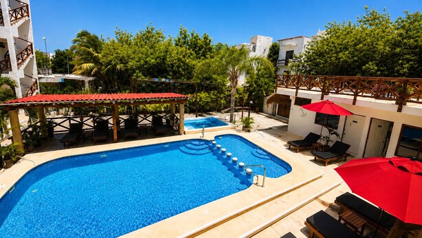 Uma piscina com estrutura de telhado vermelho, cadeiras de descanso e guarda-sóis.