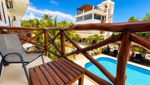 Um deck de madeira com piscina, espreguiçadeiras e vista para um edifício branco com varandas.
