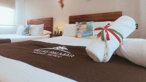 Quarto de hotel com duas camas, cabeceira de madeira, parede decorativa com figuras de pássaros e toalha com fita sobre a cama.