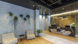 Uma área de recepção com um balcão de mármore, duas poltronas estofadas e vários vasos com plantas.