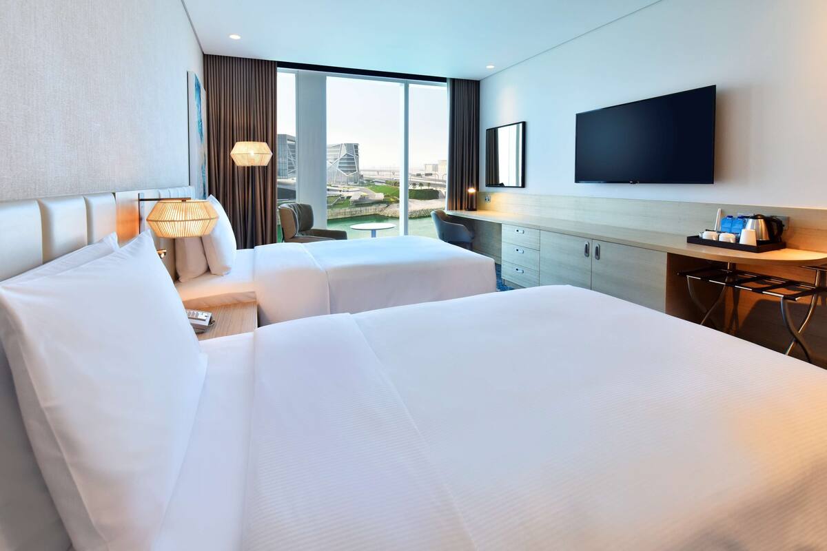 Quarto de hotel com duas camas, televisão, escrivaninha com máquina de café e vista para a cidade.