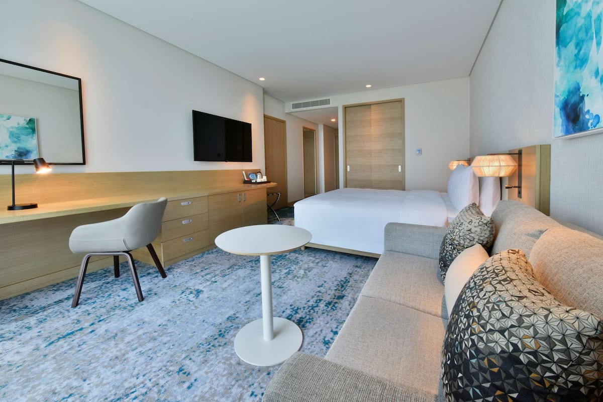Quarto de hotel moderno com cama, sofá, escrivaninha e uma pequena mesa.