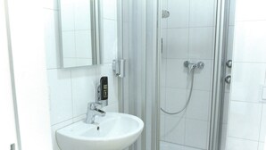Casa de banho com lavatório branco, chuveiro manual e cabine de duche com parede de vidro.