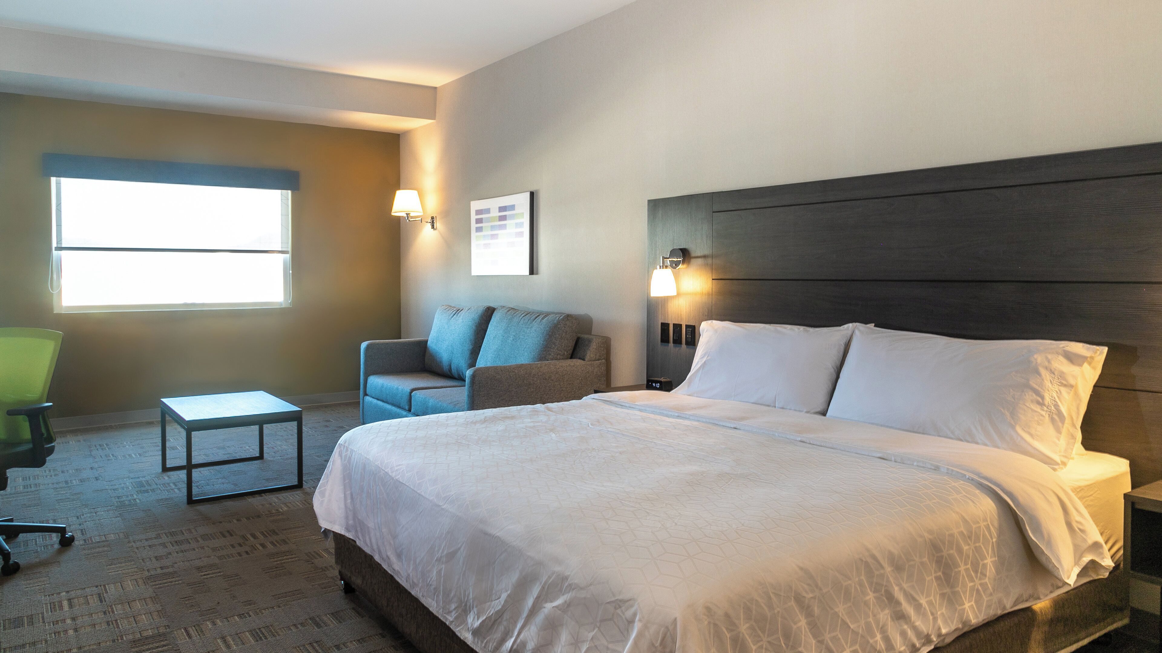 Quarto de hotel com uma cama grande, escrivaninha, cadeira, sofá e janela.