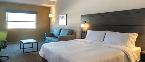 Quarto de hotel com uma cama grande, escrivaninha, cadeira, sofá e janela.