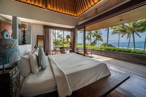 Quarto com uma cama grande, teto de madeira e vista para palmeiras e o oceano.