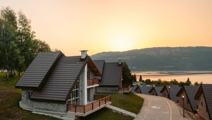 Uma fileira de casas modernas com telhados inclinados, um caminho pavimentado e vista para um lago ao pôr do sol.