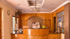 Uma área de recepção com um balcão de madeira, um candelabro, um relógio e um cartaz na parede.