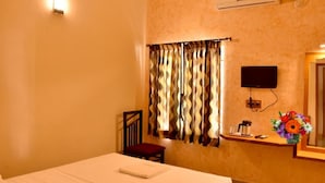 Quarto de hotel com cama, mesa de trabalho com cafeteira, televisão e espelho.