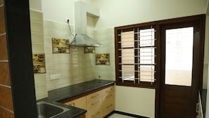 Cozinha com bancada preta, armários de madeira, pia de aço inoxidável e janela com grades.